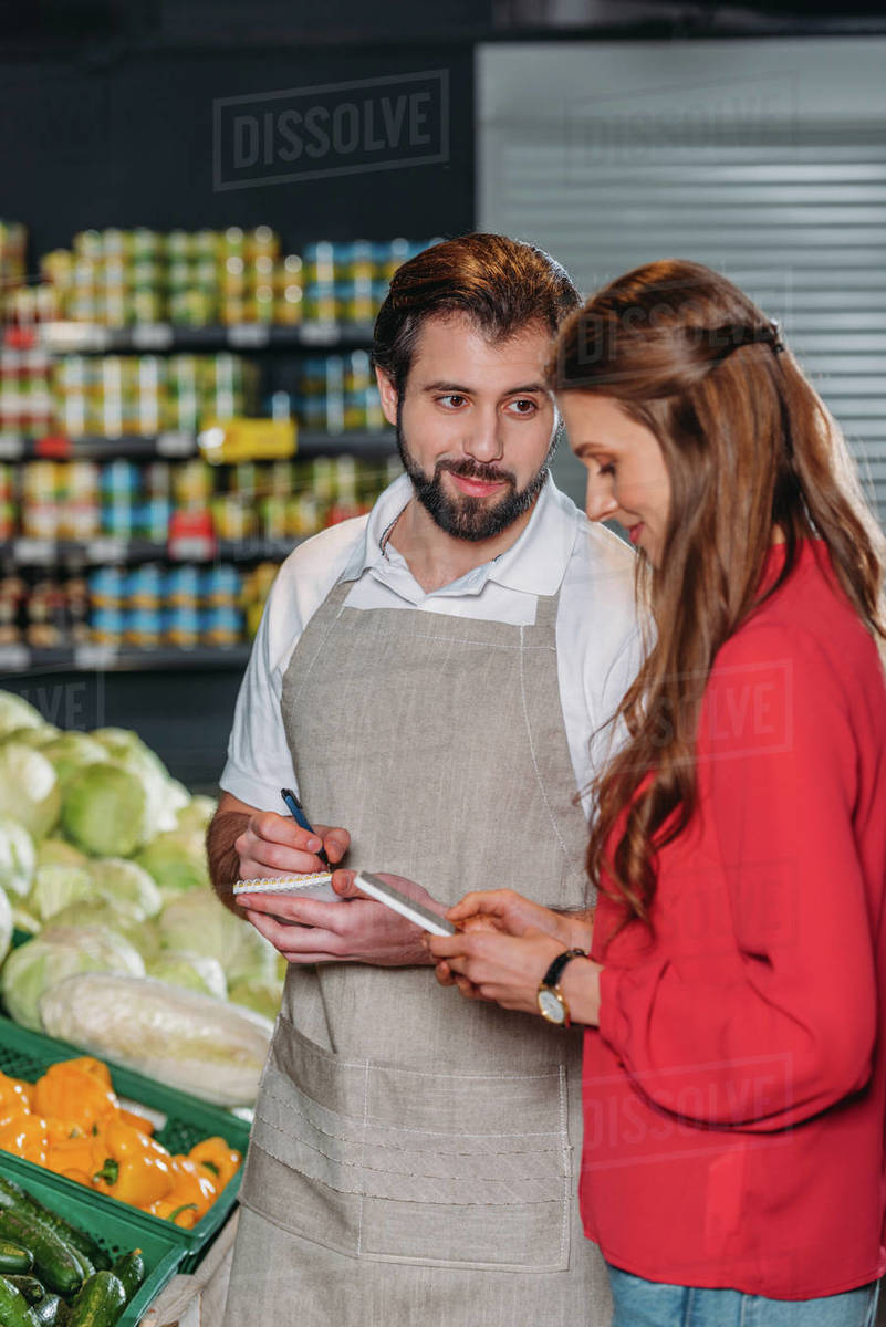 Shop assistant with notebook and female shopper in supermarket ...