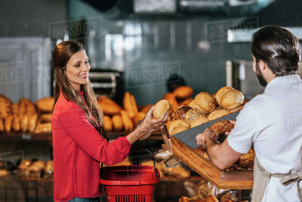 Shop assistant giving loaf of bread to woman with shopping basket in ...