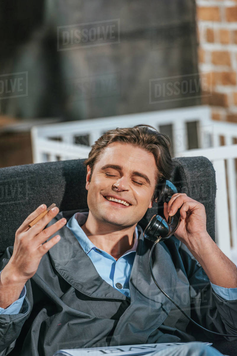Happy man in robe smoking cigarette and talking by vintage telephone ...