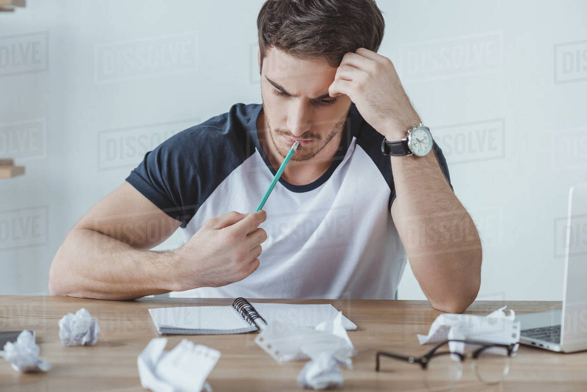 Thoughtful student studying at table with crumpled papers - Royalty ...