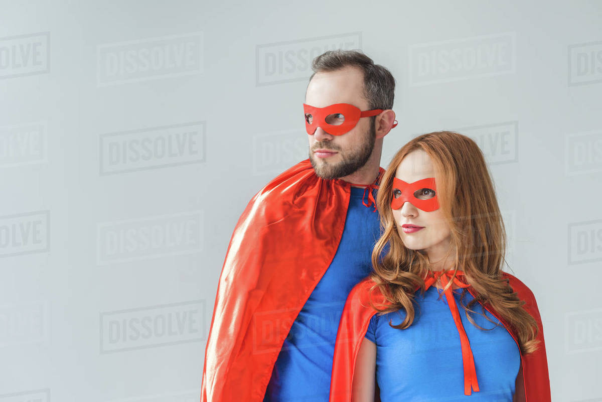 Couple in superhero costumes standing together and looking away ...