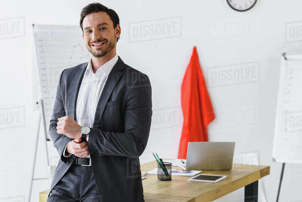 Smiling super businessman standing near table and looking at camera in ...