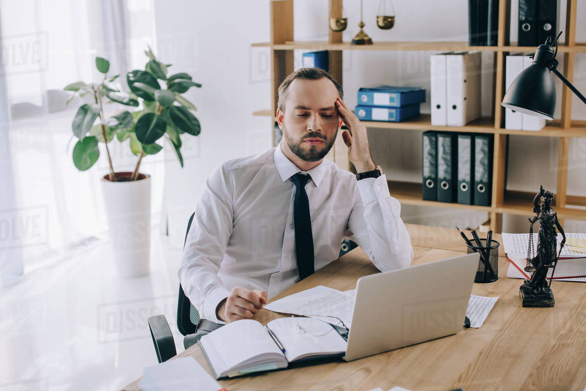 Portrait of tired lawyer sitting at workplace with laptop and documents ...