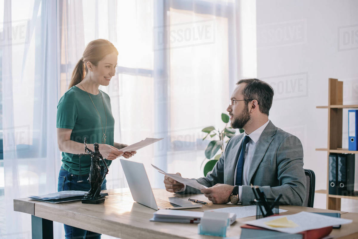 Lawyer and smiling client discussing contract at workplace with laptop ...