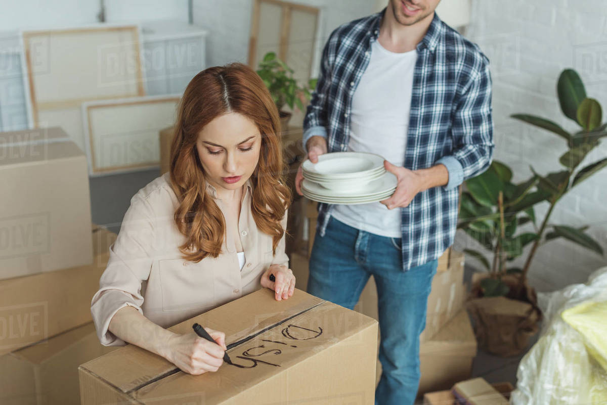 Partial view of woman signing cardboard box with husband with dishes ...