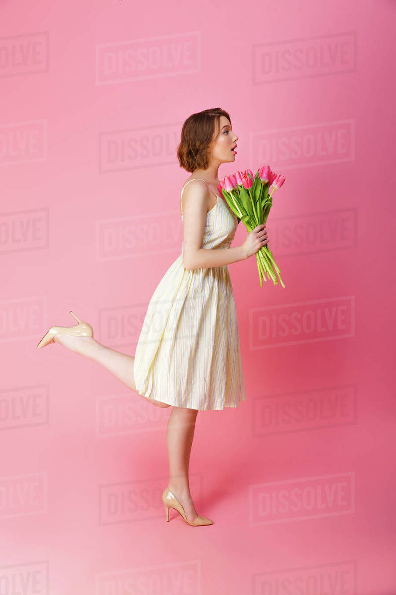 Side view of young woman in white dress with bouquet of pink tulips ...