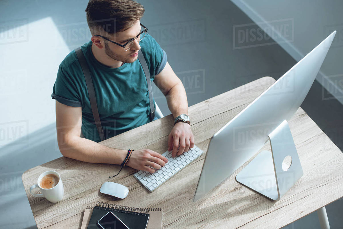 Overhead view of young man in eyeglasses typing on keyboard and working ...