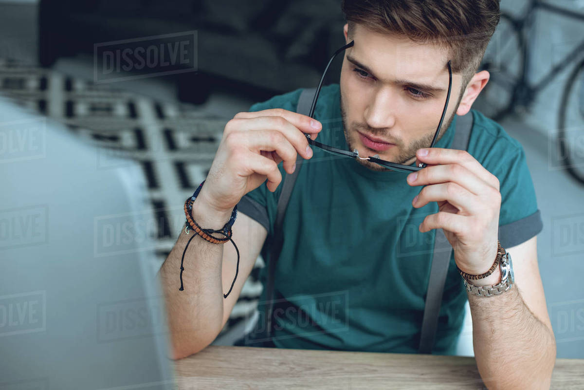 Focused young man wearing eyeglasses and using desktop computer at home ...