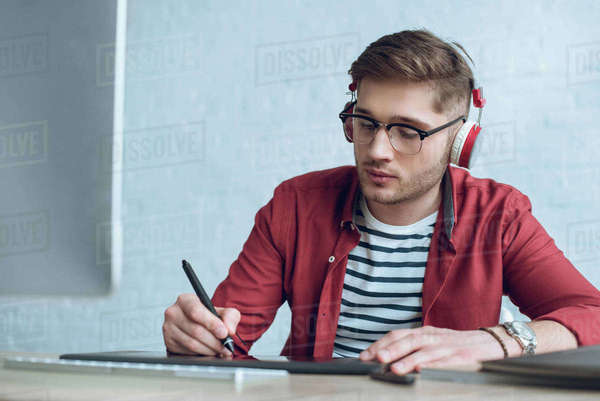 Freelancer man in headphones drawing with graphic tablet by table with ...