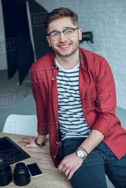 Smiling young man leaning on table with camera lenses - Royalty-free ...