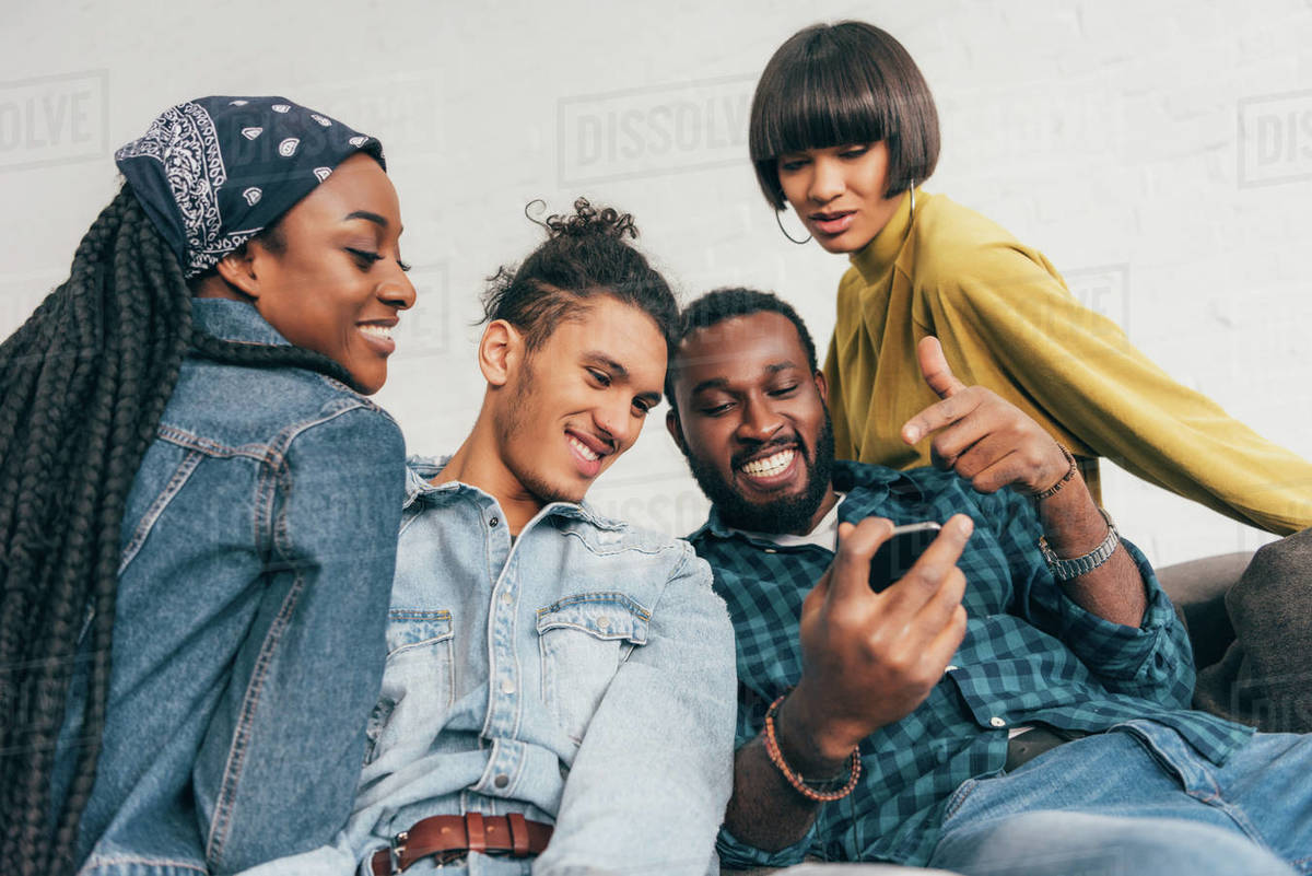 Young black man pointing at smartphone screen to smiling friends ...
