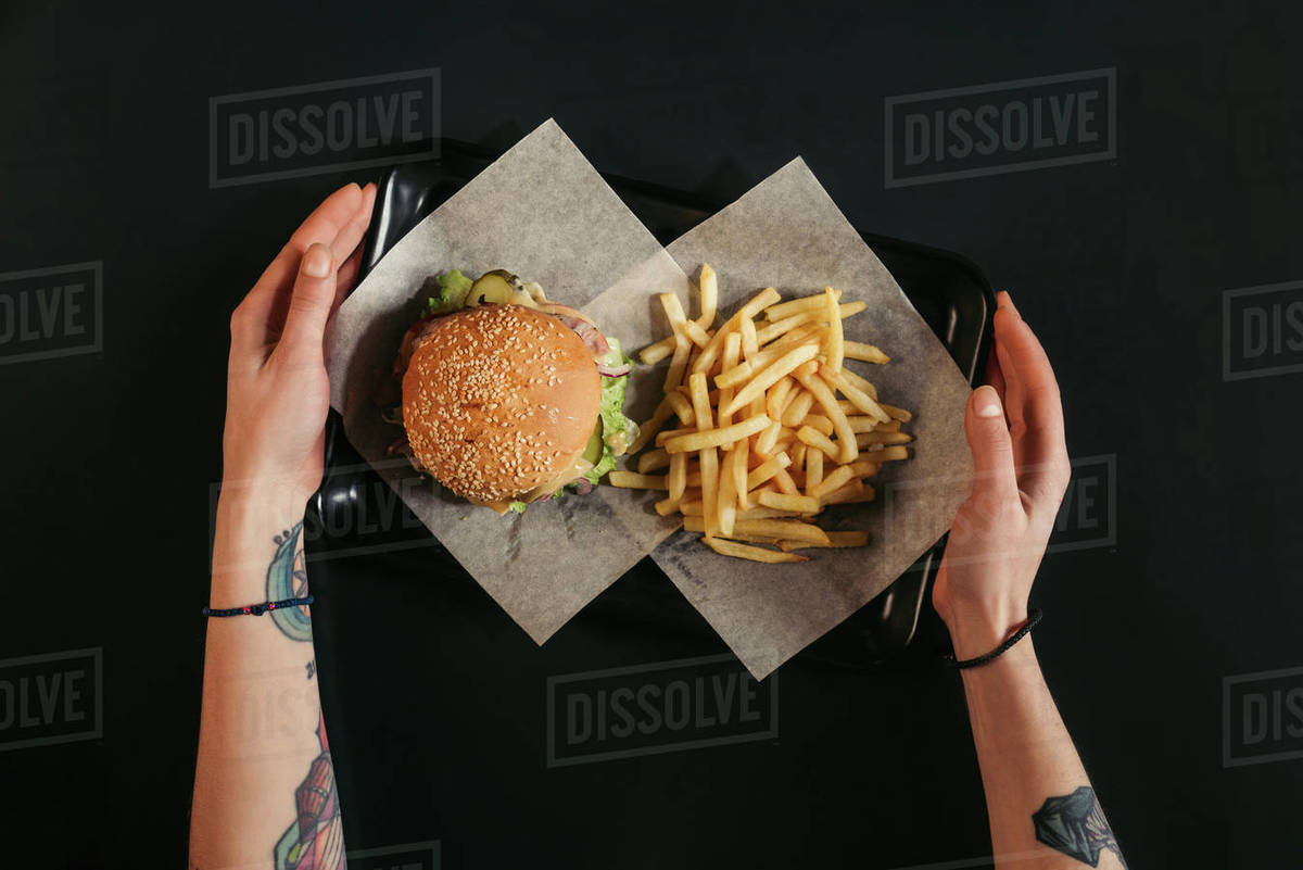 Cropped shot of human hands holding tray with delicious burger and ...