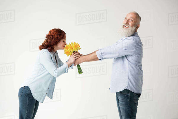 Smiling senior man giving bouquet of daffodils to his wife, isolated on ...