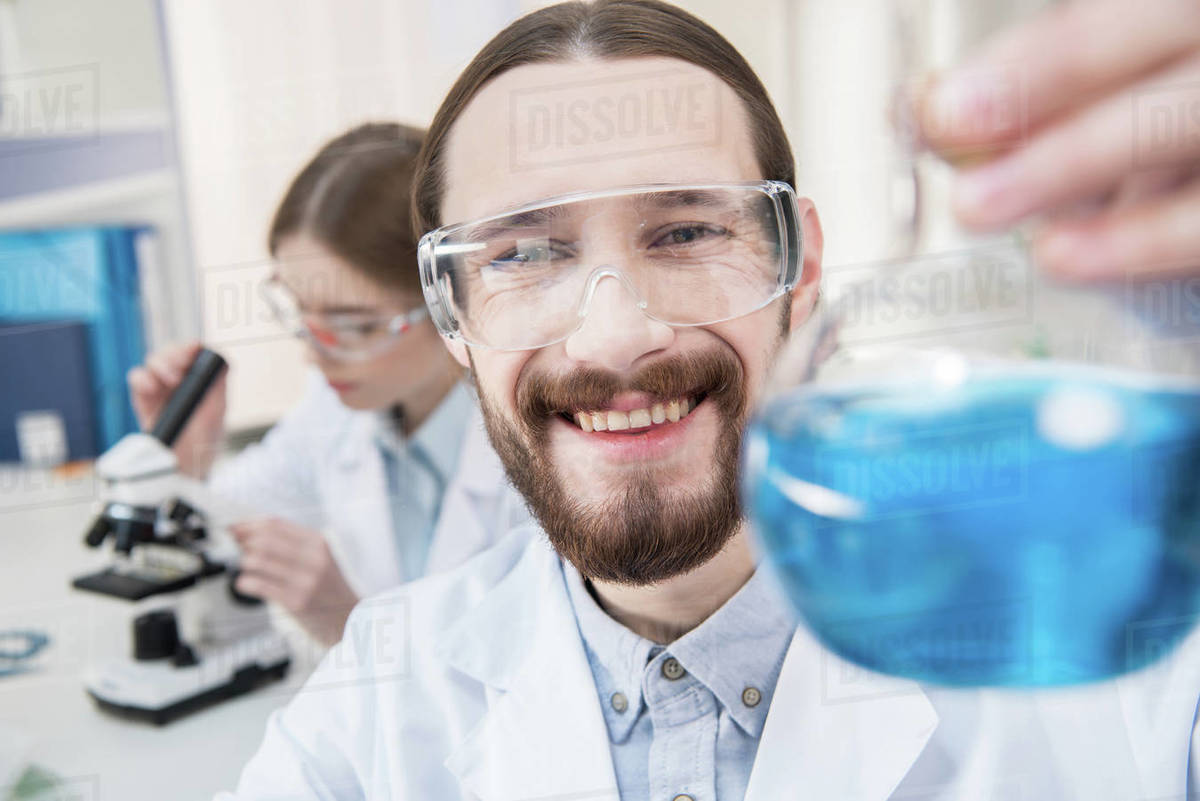 Smiling young scientist holding flask with chemical reagent - Royalty ...