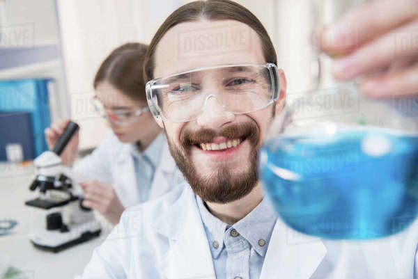 Smiling young scientist holding flask with chemical reagent - Royalty ...