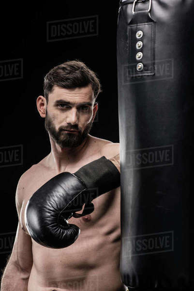 Young muscular boxer leaning on punching bag and looking at camera ...