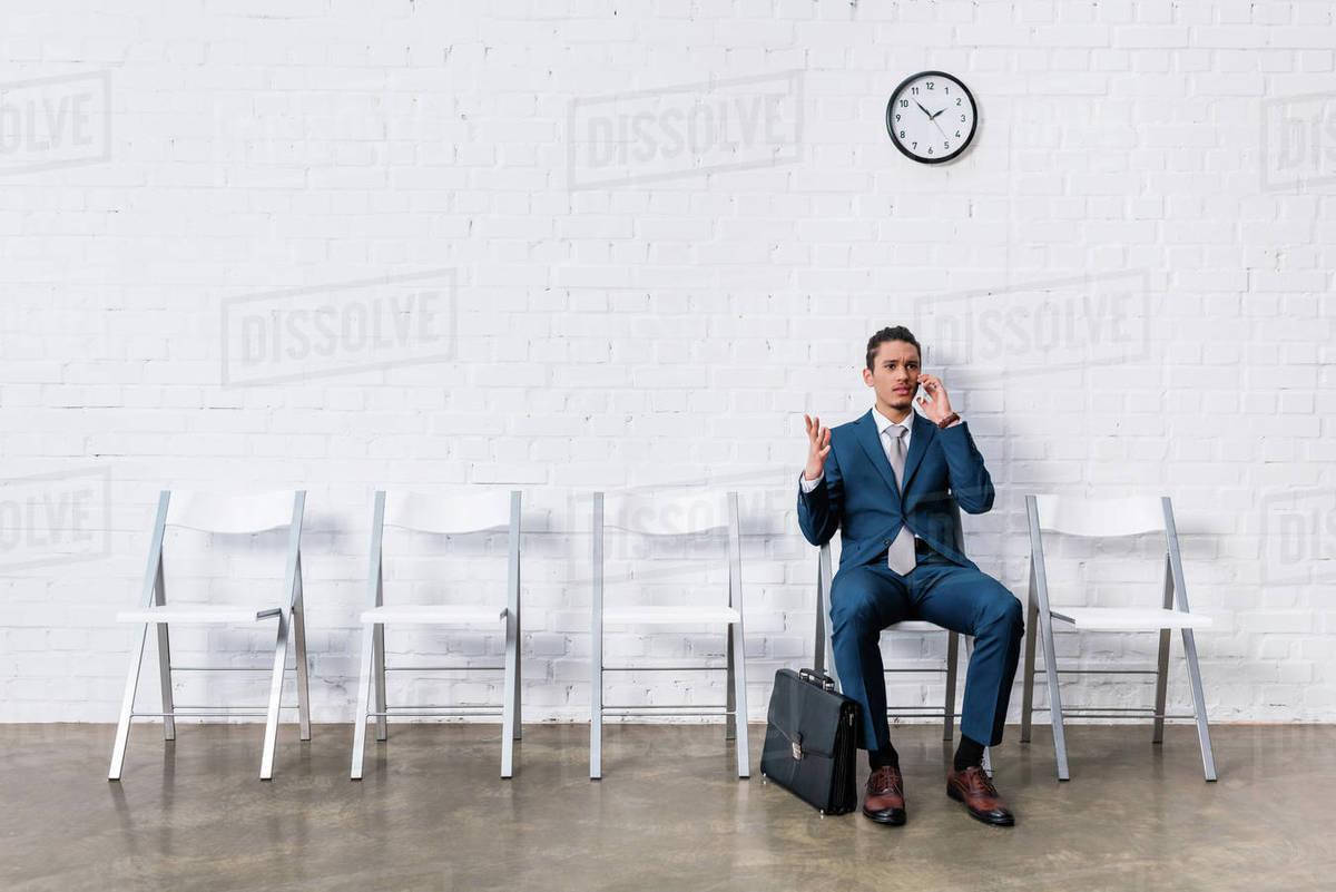 Businessman talking on phone while sitting and waiting on chair ...