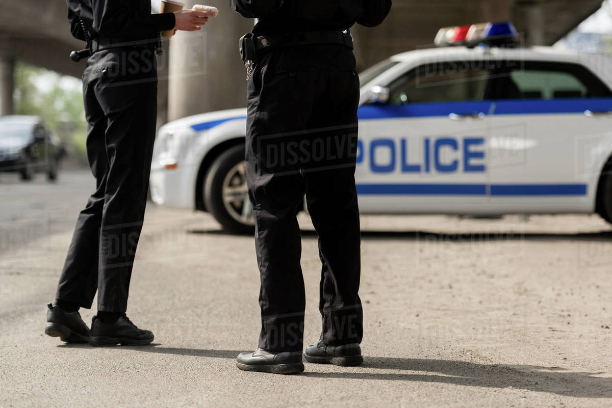 Cropped shot of police officers standing in front of police car ...
