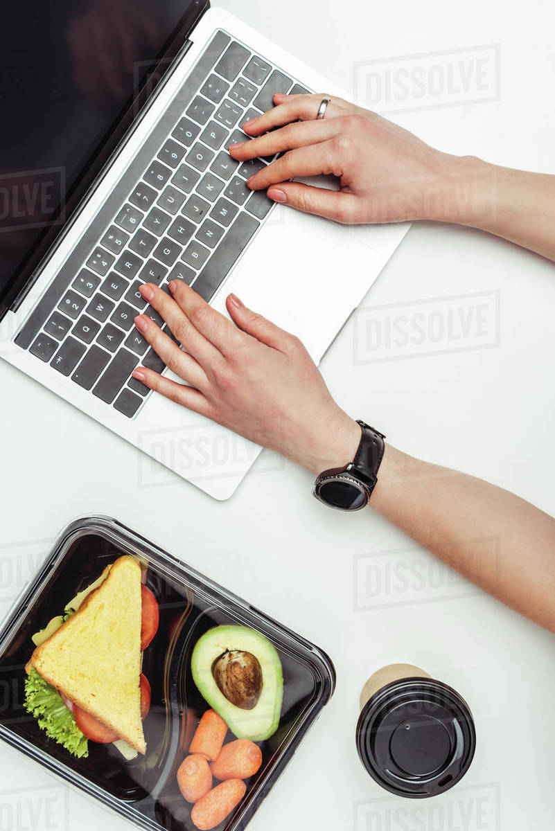 Cropped image of woman using laptop at table with food in lunch box ...