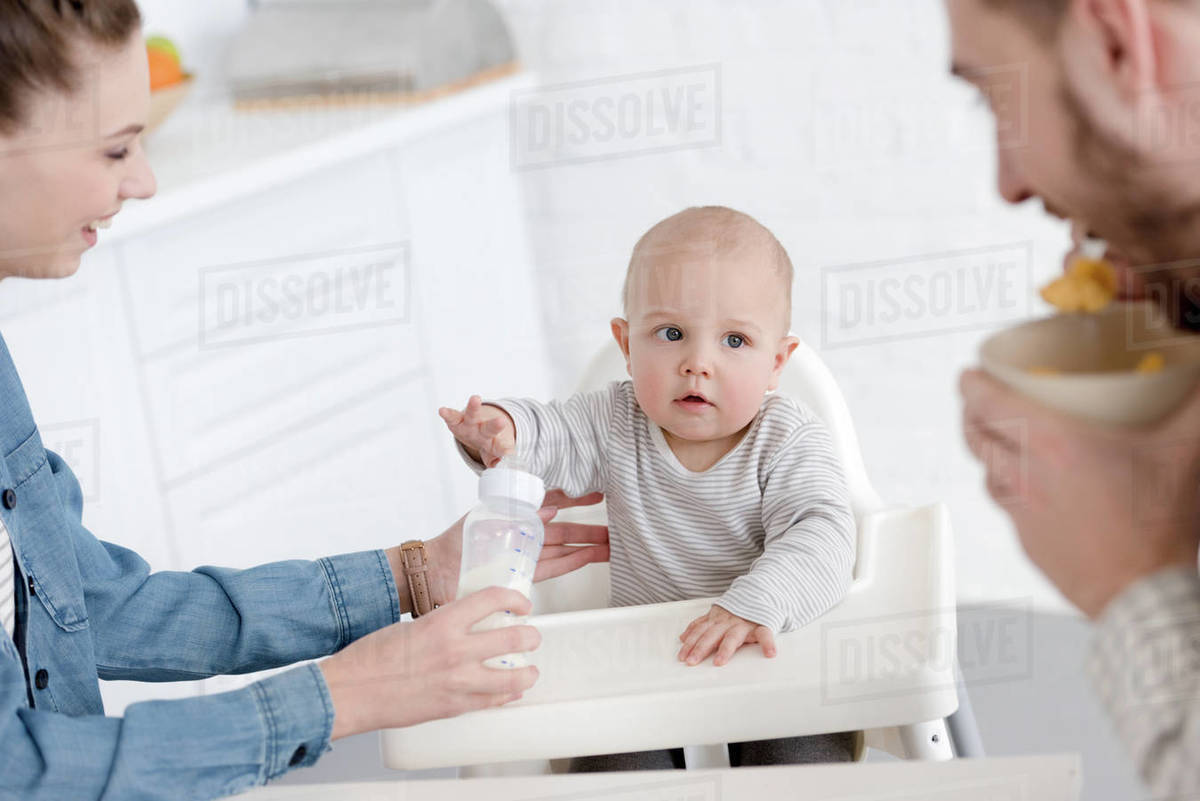 Parents feeding baby boy with milk in baby bottle on kitchen - Royalty ...