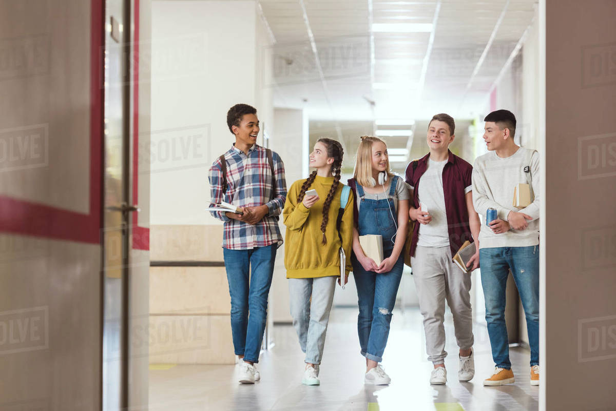 Group of smiling high school classmates walking by school corridor ...