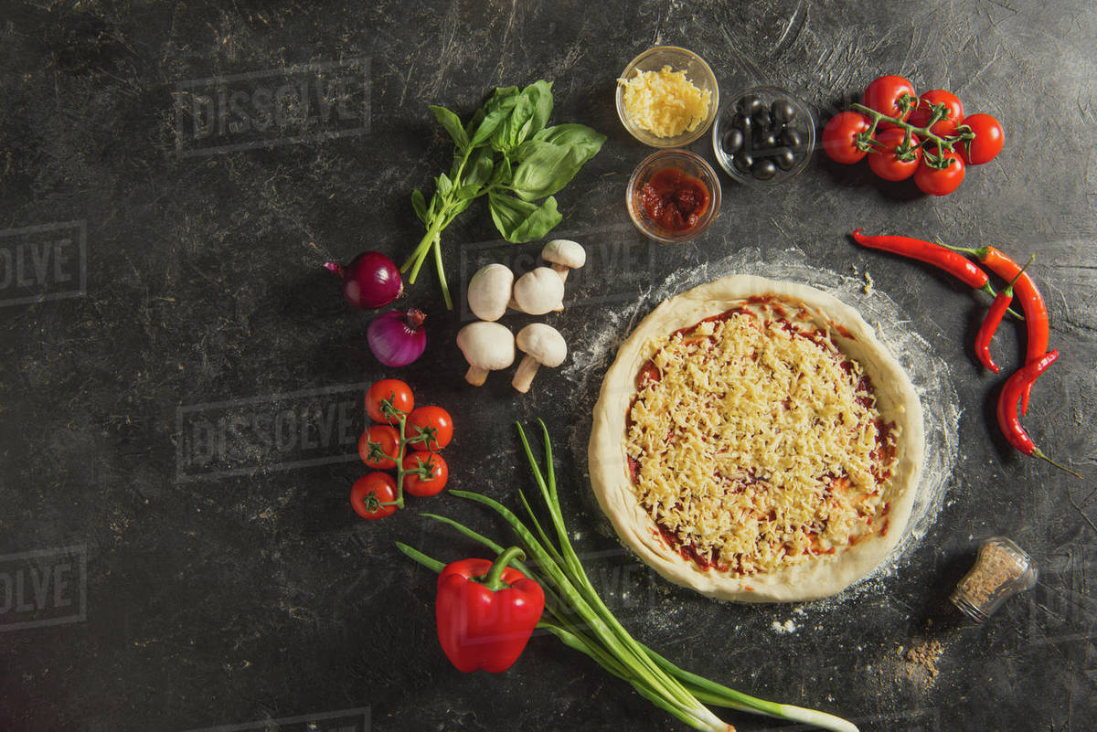 Top view of raw Italian pizza and fresh ingredients around on dark ...