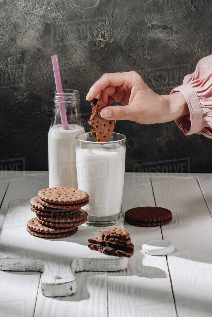Cropped shot of woman dipping delicious cookie into glass of milk ...