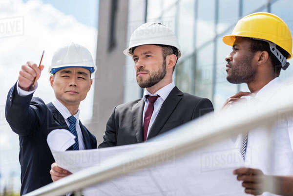 Professional architects in hardhats working with blueprint outside ...
