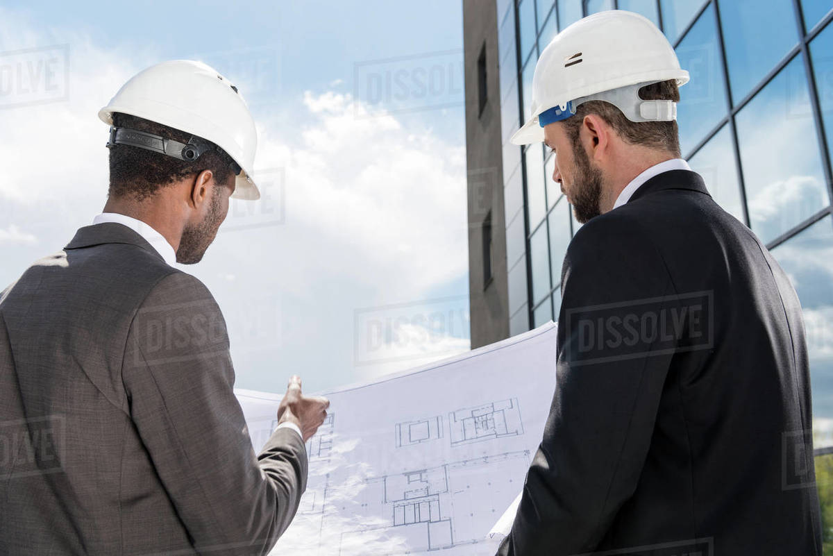 Back view of professional architects in hardhats working with blueprint ...