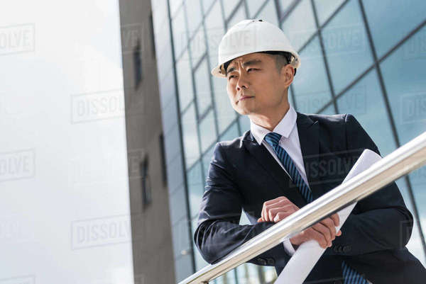portrait of pensive professional architect in hard hat holding ...