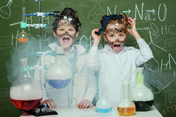 Little kids in white coats with chalkboard behind in science laboratory ...