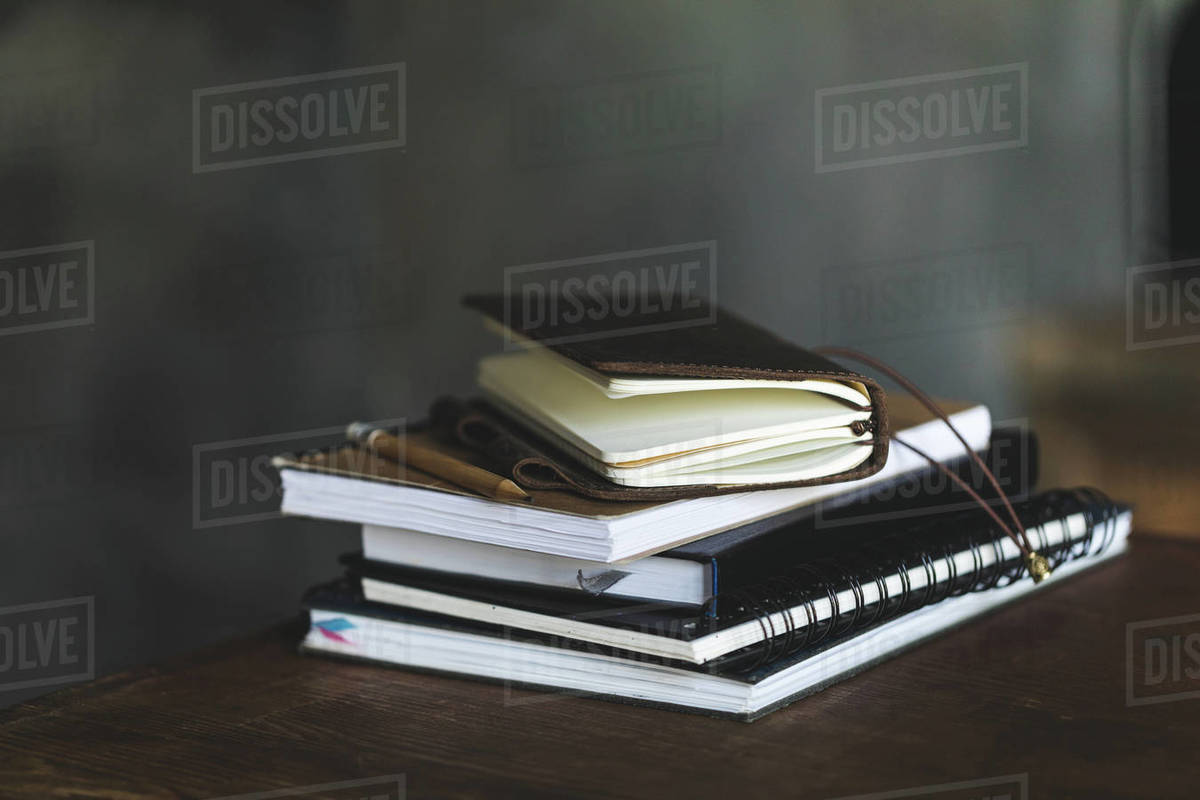 Close-up view of stacked notebooks and pencil on dark table - Royalty ...
