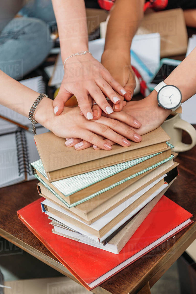 Close-up view of young women stacking hands on pile of books - Royalty ...