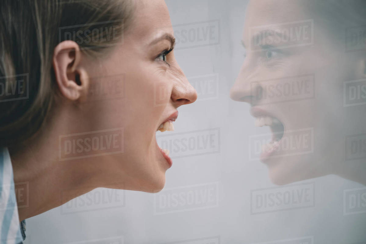 Aggressive stressed woman screaming at her reflection in mirror ...