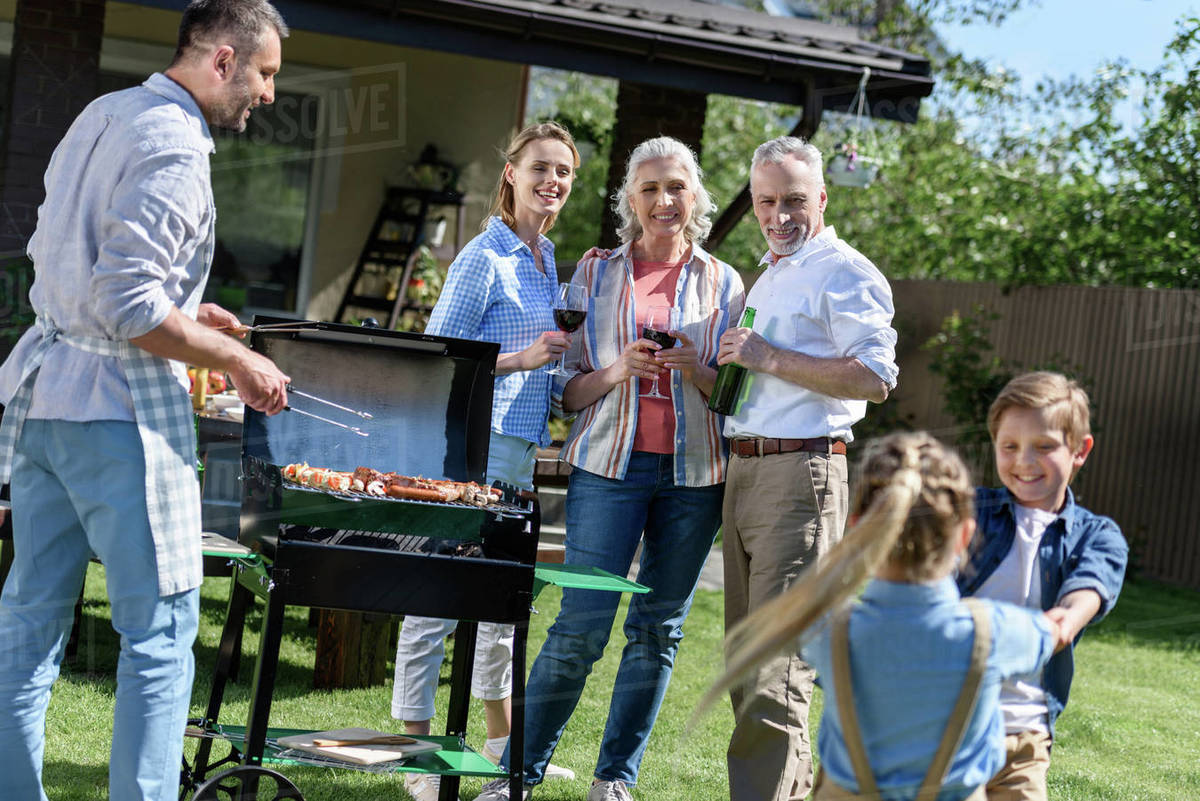 smiling man cooking food on barbecue with family enjoying weekend near ...