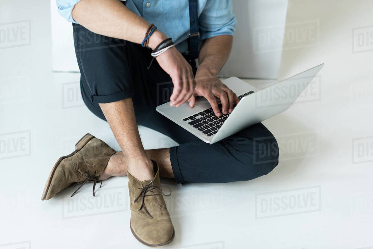 Stylish young man sitting and using laptop on grey - Royalty-free Stock ...