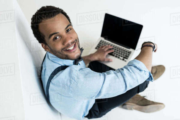 Handsome young man using laptop with blank screen and smiling at camera ...