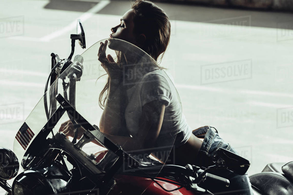 Side view of sensual young brunette woman posing on motorcycle ...
