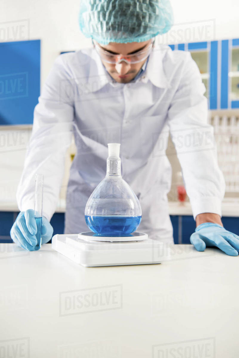 Young pharmacy worker weighing a flask with reagent in laboratory ...