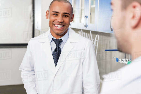 Young african american doctor in lab coat smiling and looking at camera ...