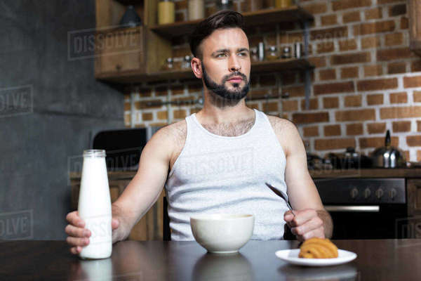 Handsome young man pouring milk from bottle at breakfast - Stock Photo ...