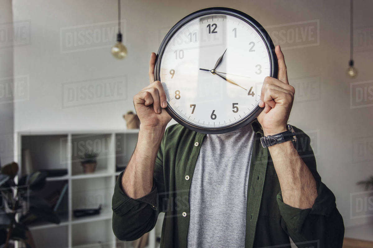 Young man holding wall clock while standing in office - Royalty-free ...