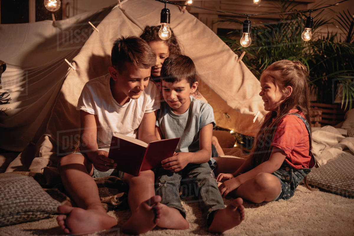 Multicultural group of smiling children reading book at home - Royalty ...