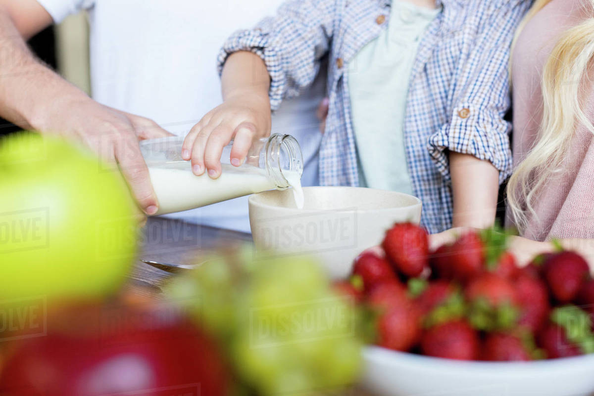 Cropped shot of parents with child pouring milk into bow for breakfast ...