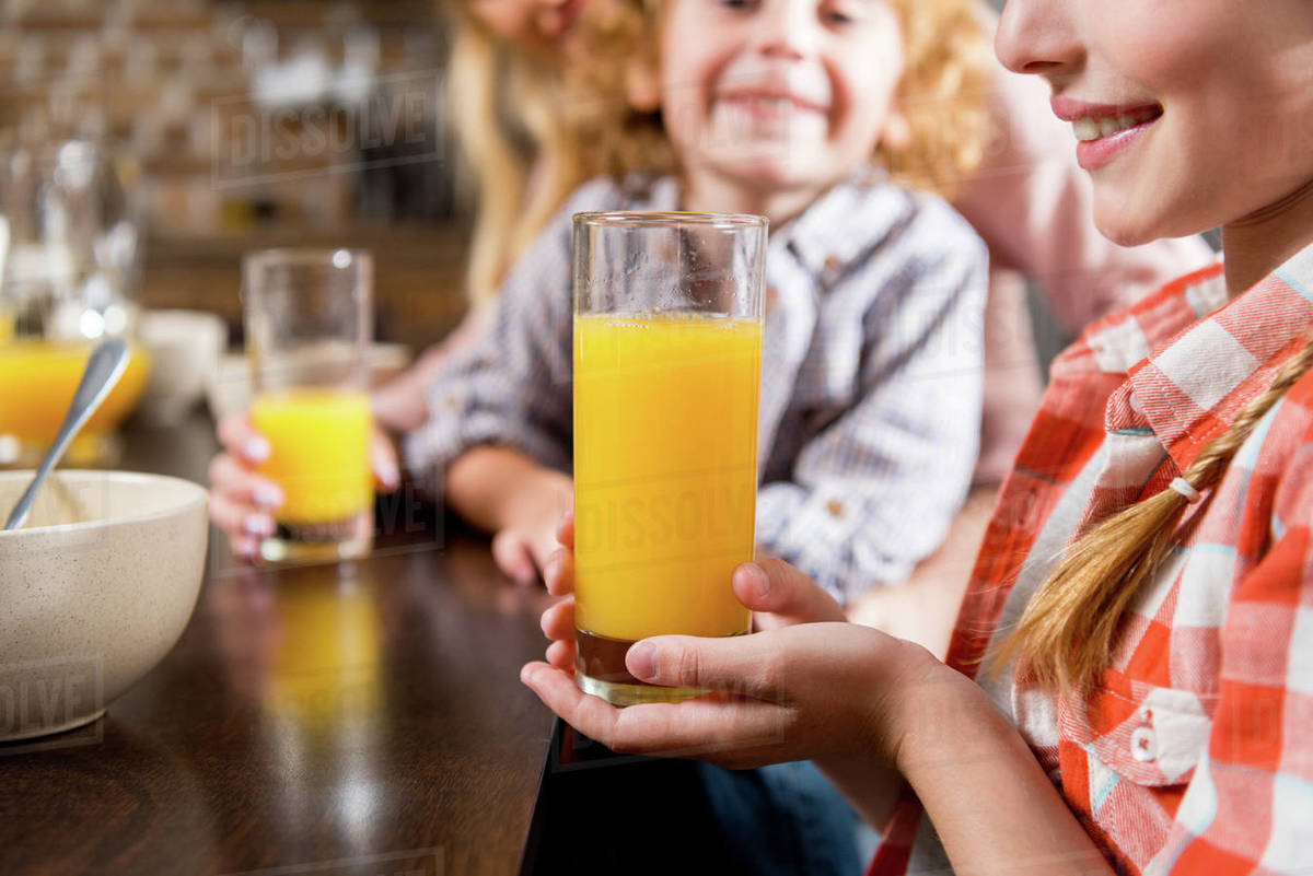 Cropped shot of cute little kids drinking orange juice at breakfast ...