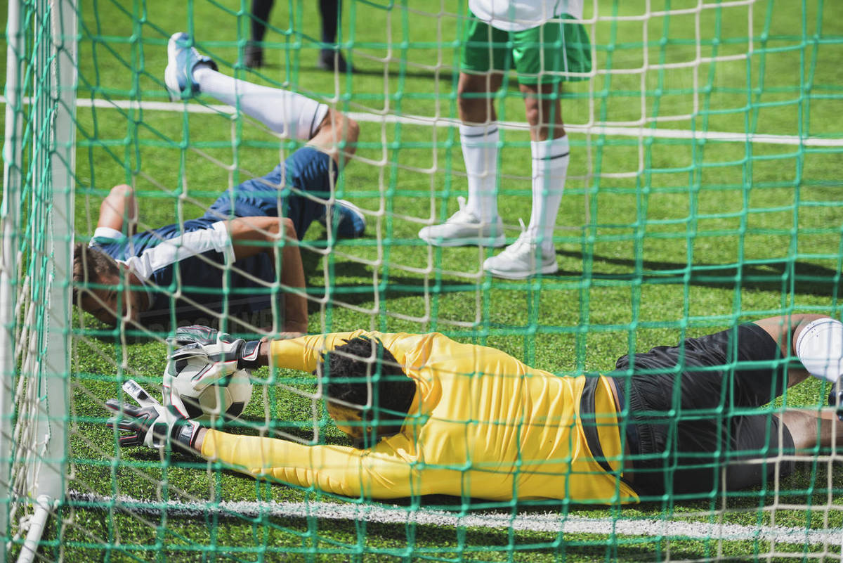 Back view of goalkeeper catching ball during soccer game on pitch ...