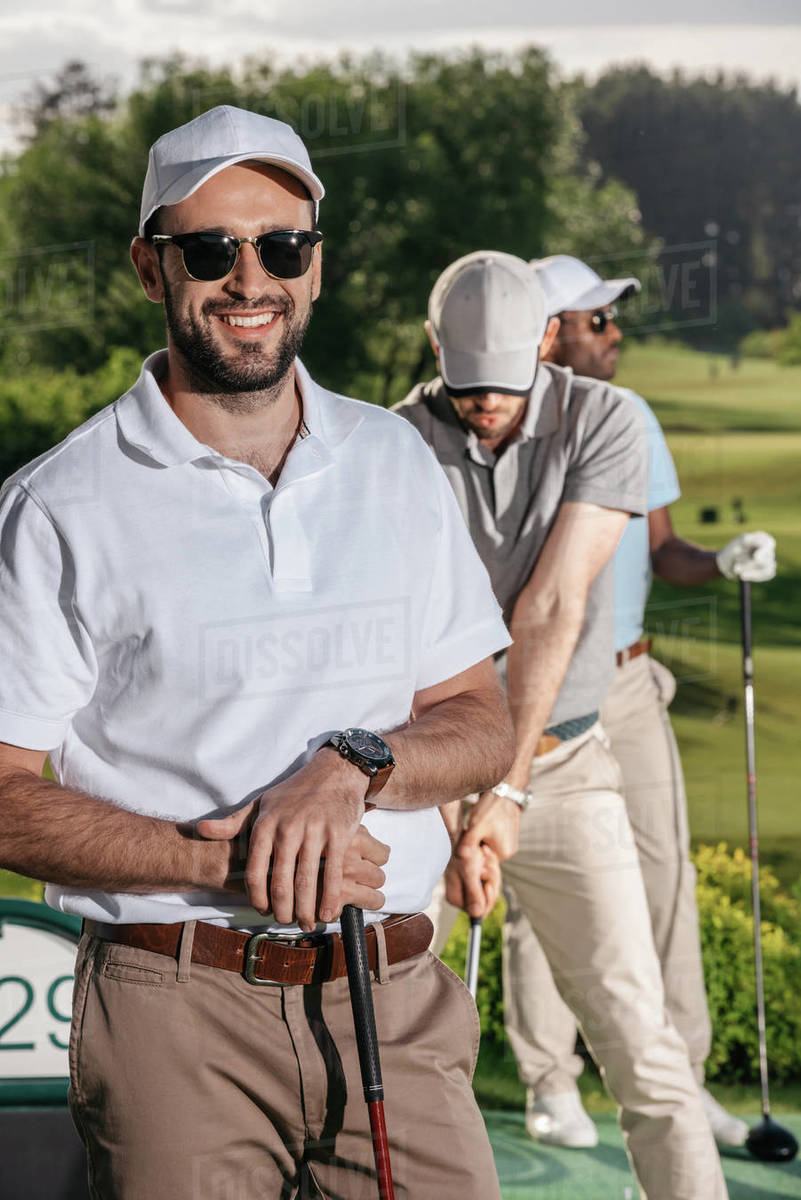 Portrait of smiling golfer looking at camera while men playing golf ...