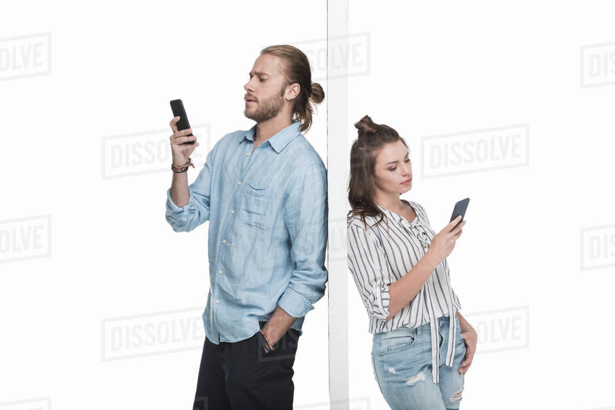 Young couple using smartphones while standing separated by wall ...