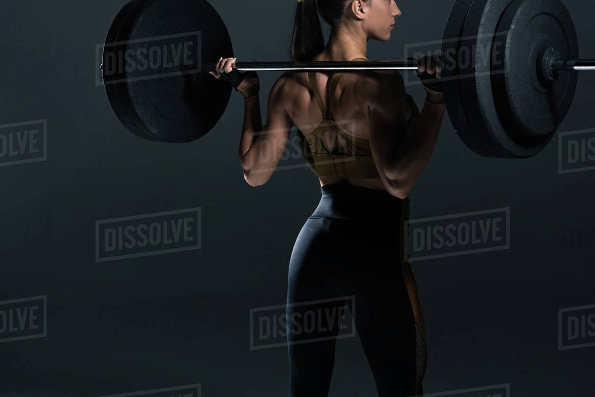 Back view of female bodybuilder posing with barbell, isolated on grey ...