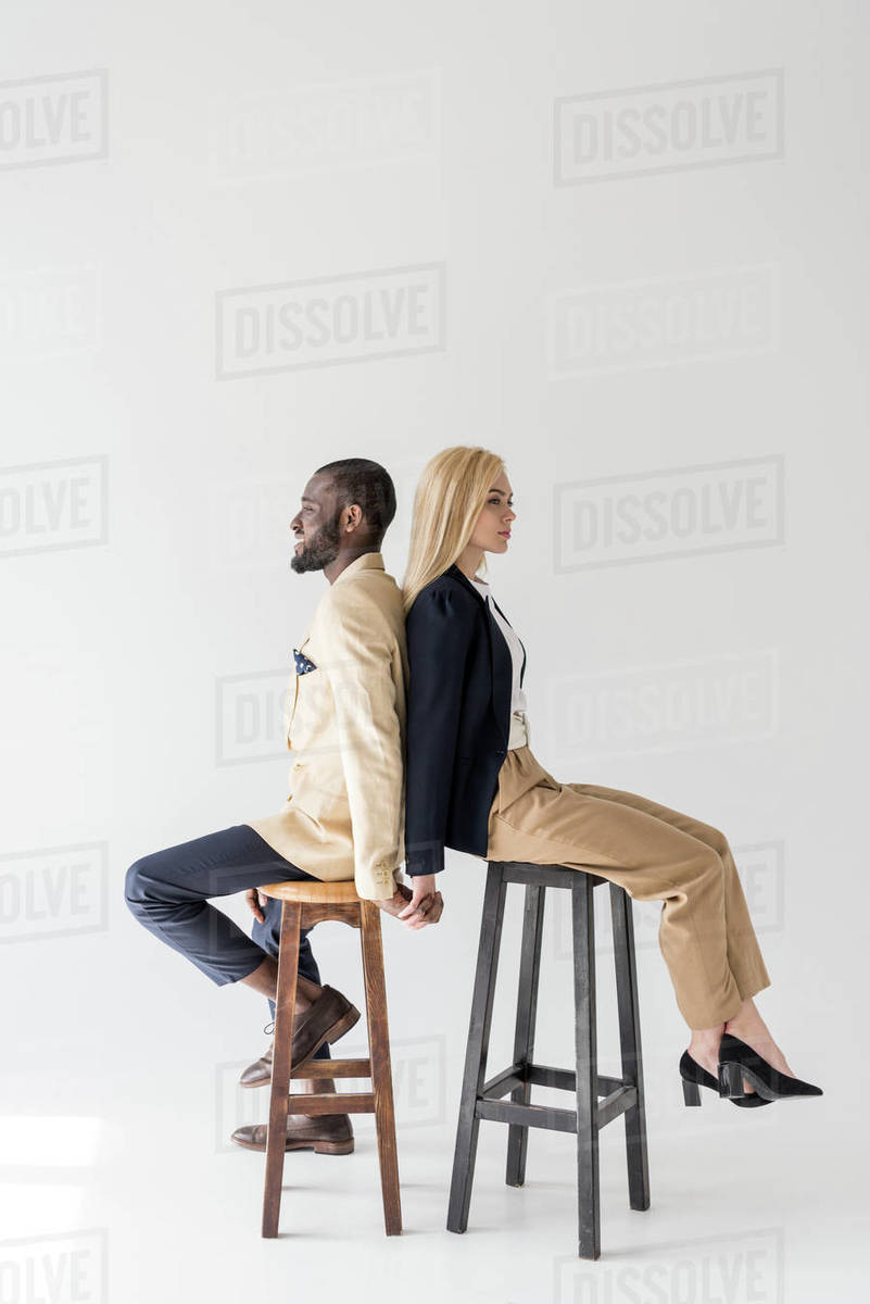 Side view of fashionable young multiethnic couple sitting back to back ...